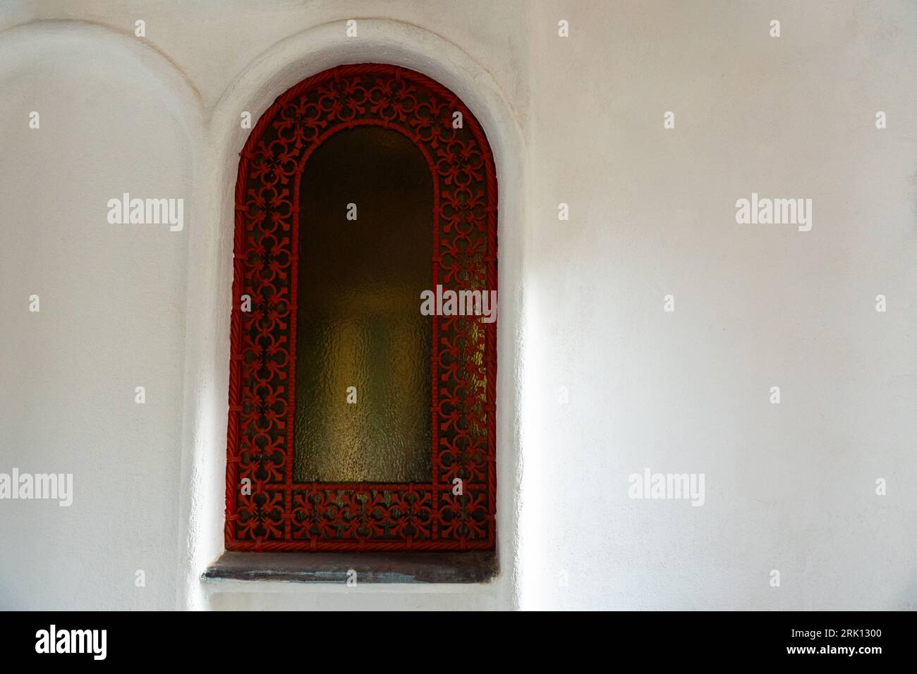 Arched window with red iron decorated frame set in white wall building ...