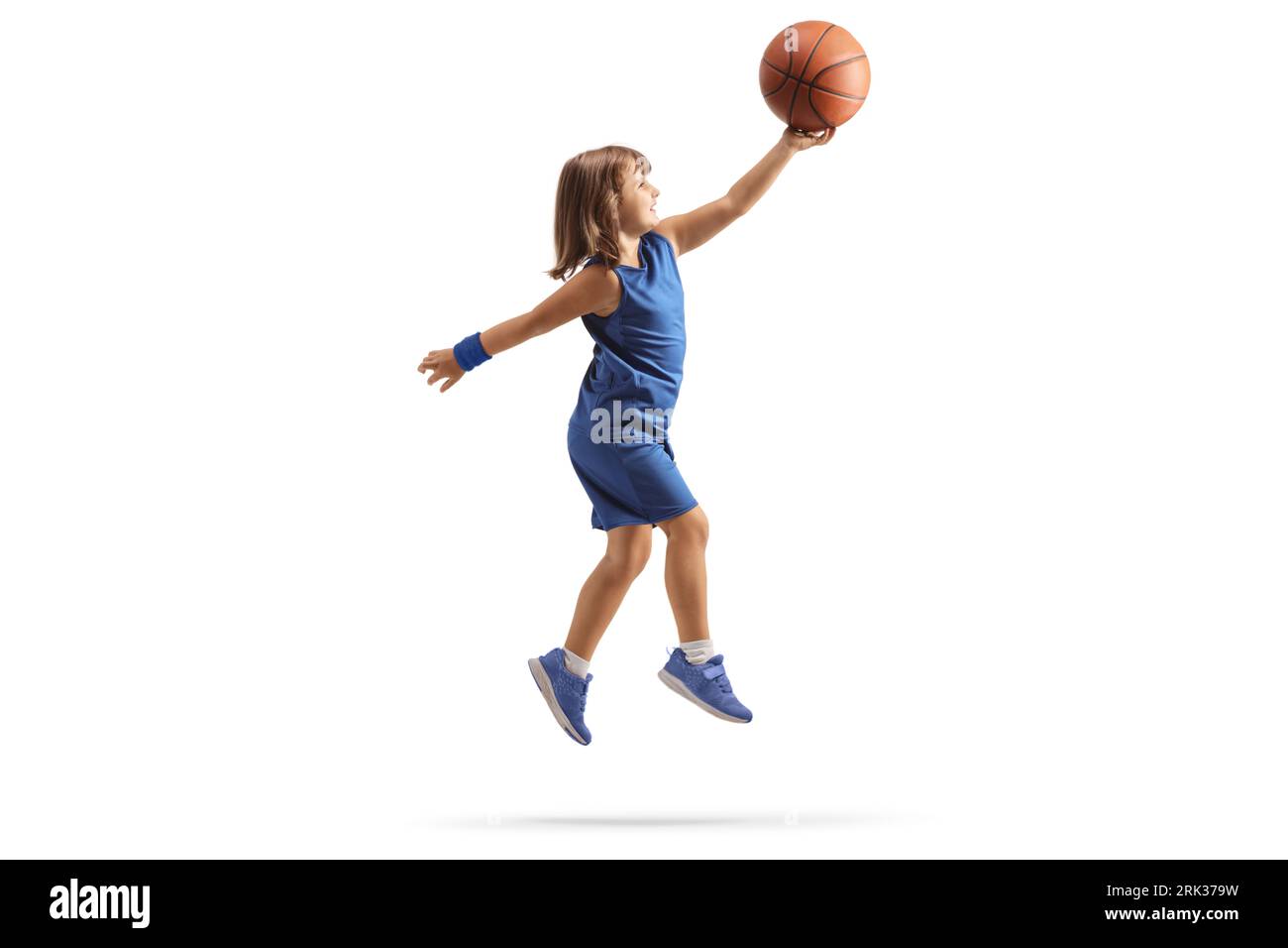Little girl in a blue sports jersey shooting a layup isolated on white ...