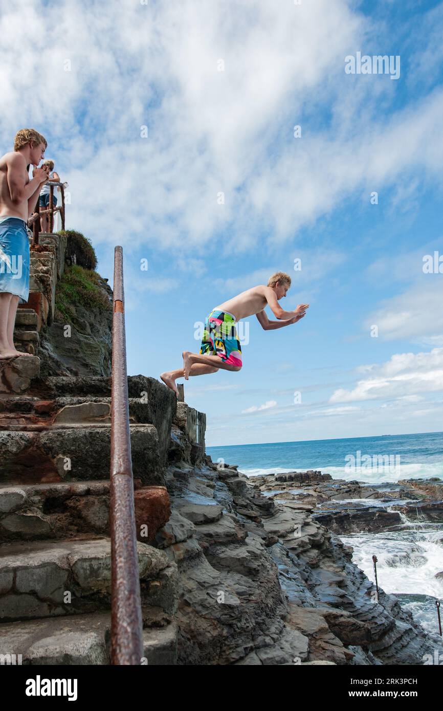 a group of teenage boys jumping into and play in a natural rock pool in ...