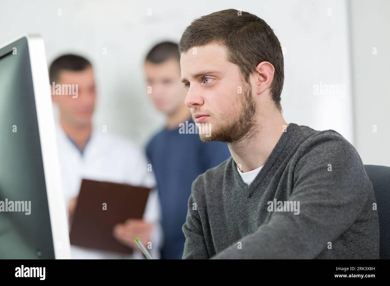young man using computer teacher and fellow student in background Stock ...