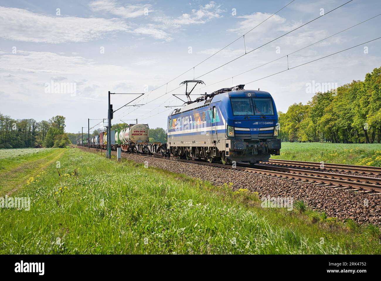 A blue train chugging down a set of tracks in a rural landscape Stock ...