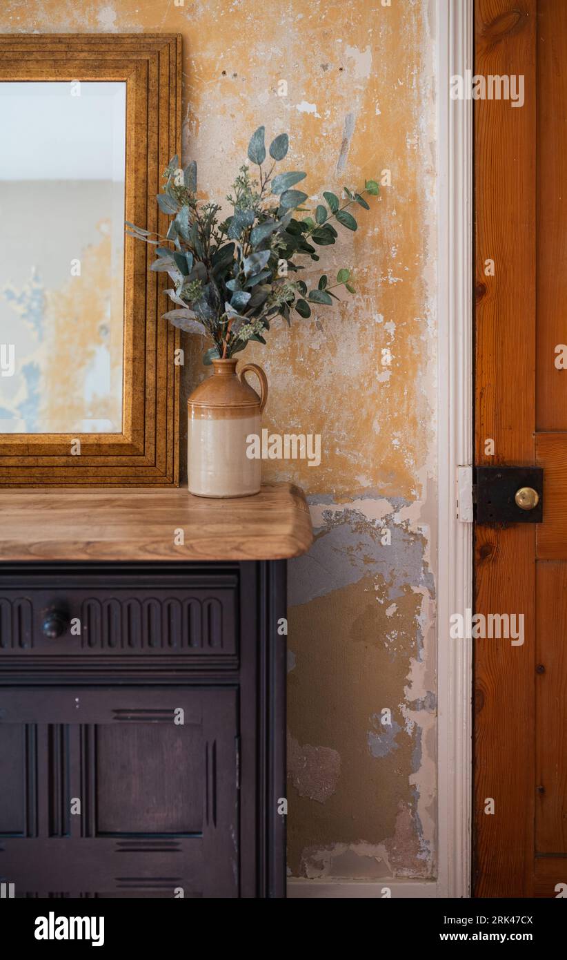 A rustic hallway counter with a mirror and a jug with leafy branches ...