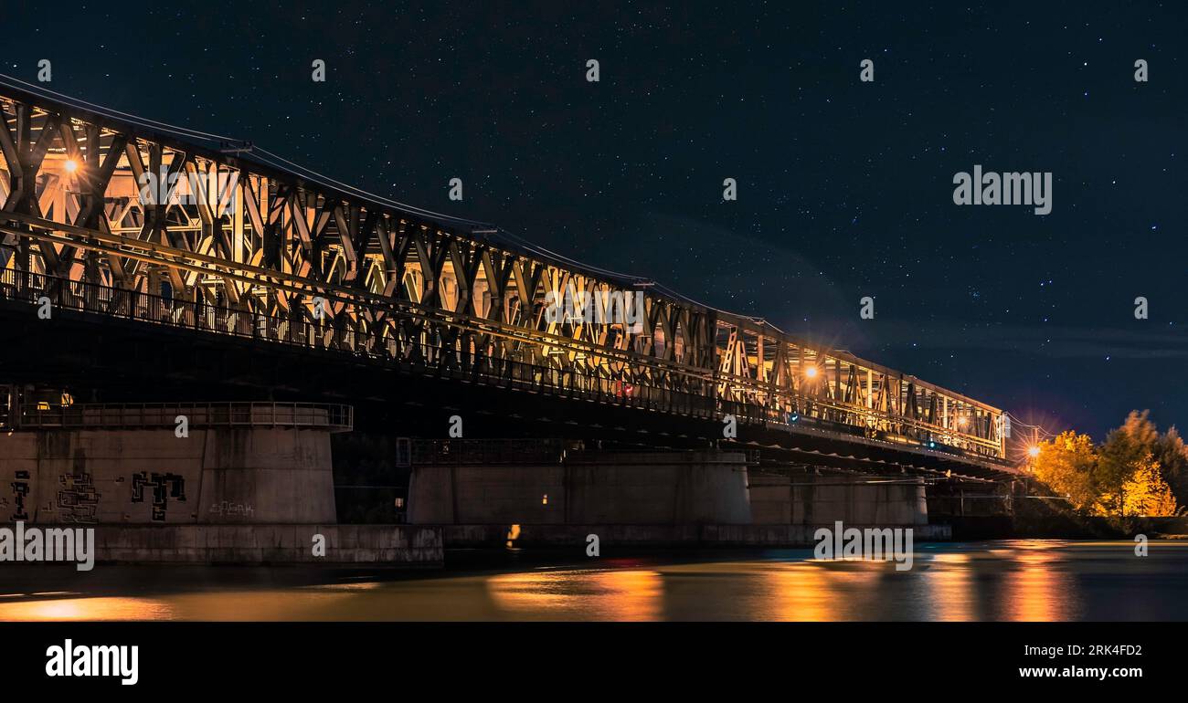 A train travelling over a bridge spanning a river in a night-time ...