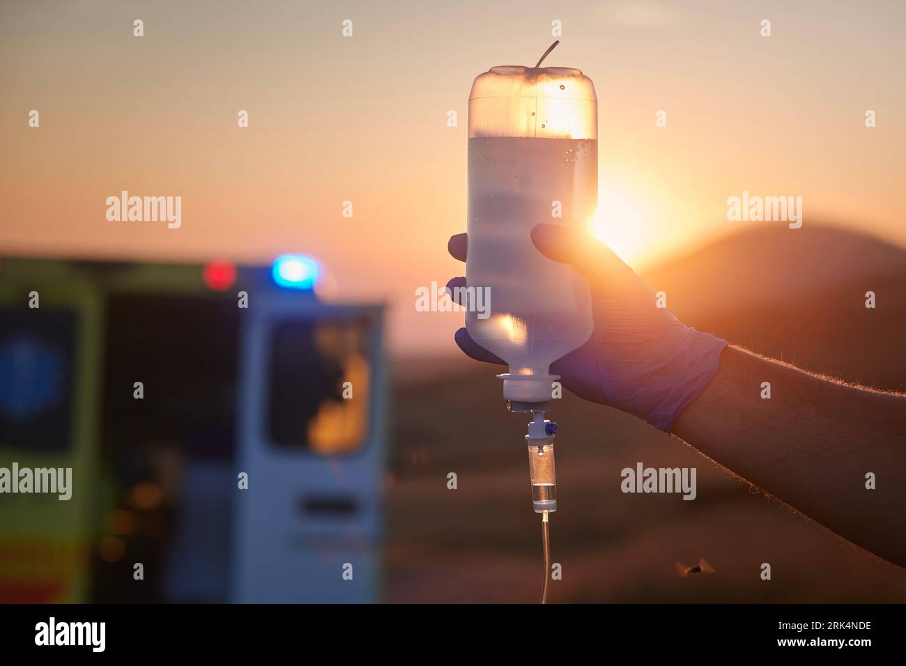 Close-up hand of paramedic holding infusion set against ambulance car ...