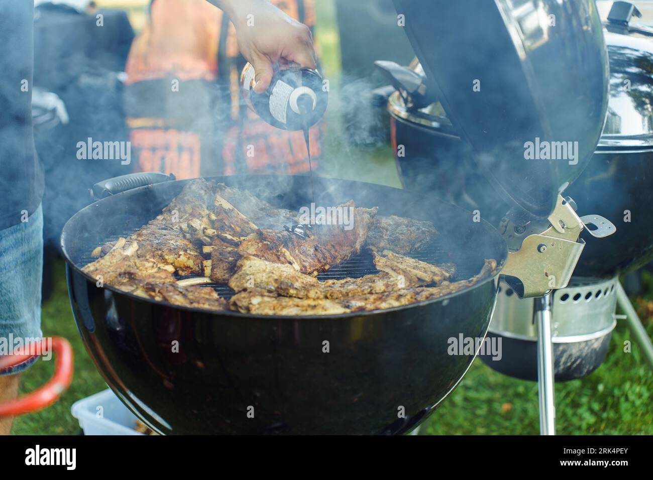 A cook pours sauce over grilled ribs during a barbecue party in the ...