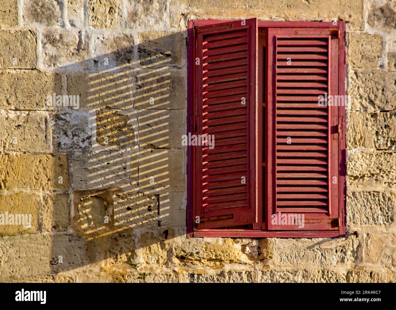 A red wooden louvered window with a shadow cast across the frame from ...