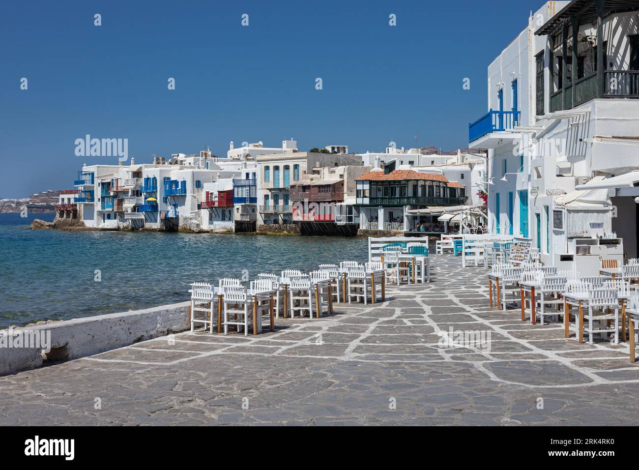 A row of wooden tables and chairs are situated along a paved stone ...