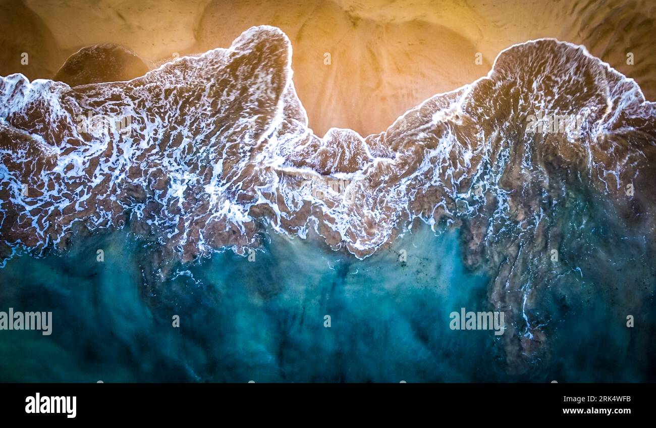 An aerial view of a picturesque beach surrounded by crystal blue waves lapping against the ...