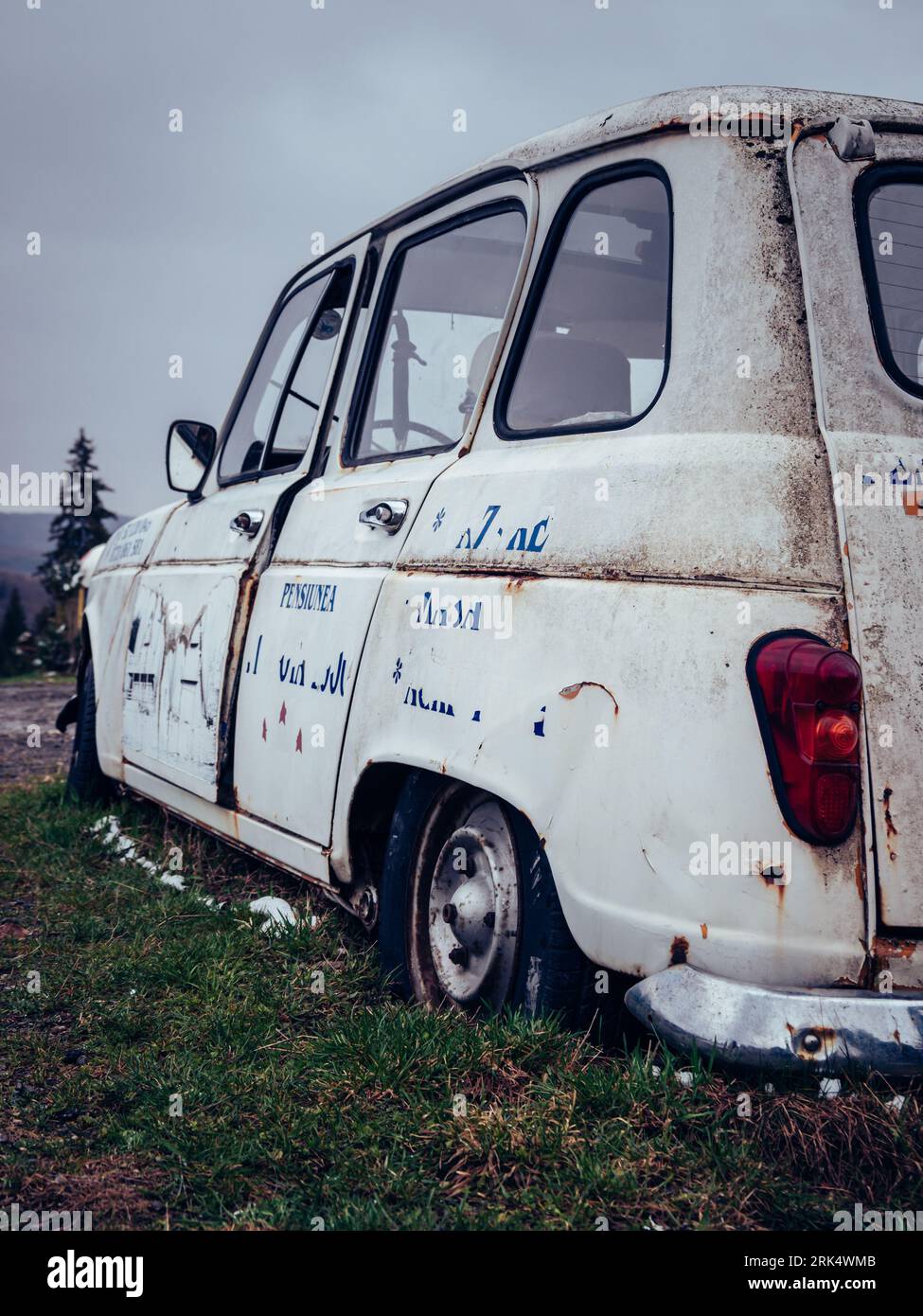An aged, rusted automobile situated in an expansive grassy meadow, its ...