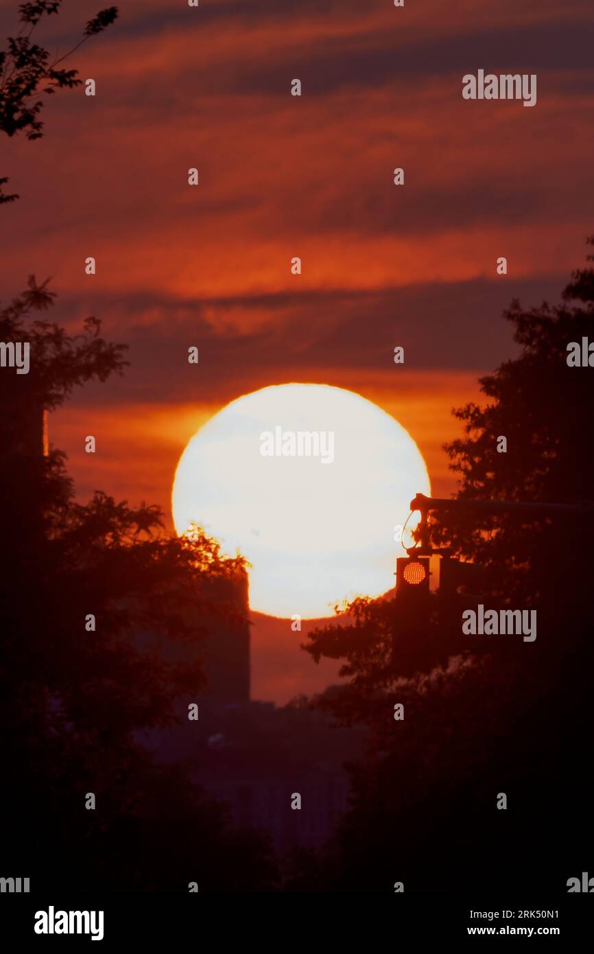 A red sun at sunset, glowing in the sky and casting a deep orange hue ...