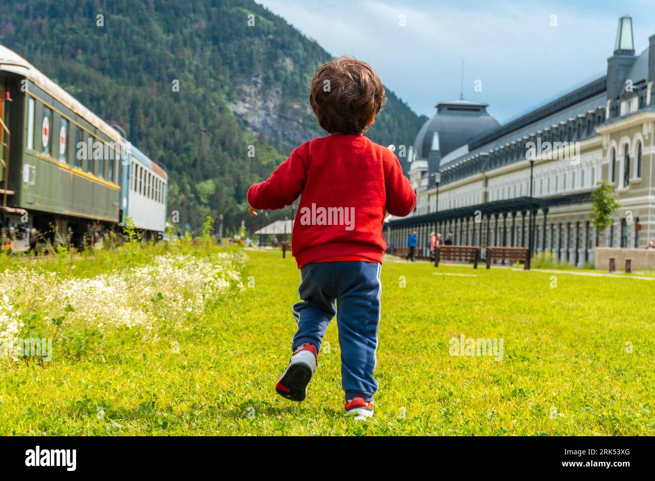 A young boy with a cheerful expression sprints across a vast grassy ...