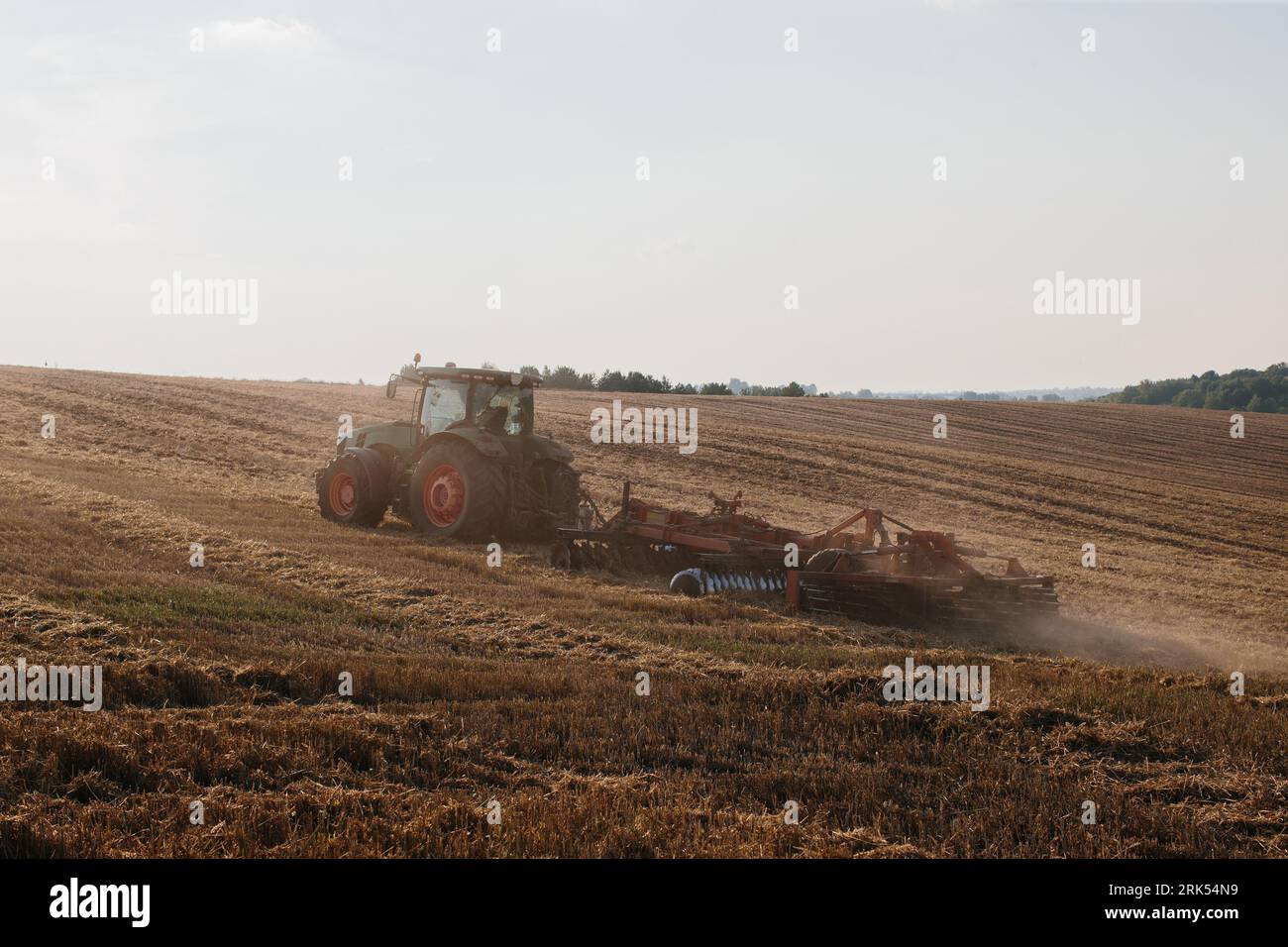 A modern tractor with a heavy trailed disc harrow plows a wheat field ...