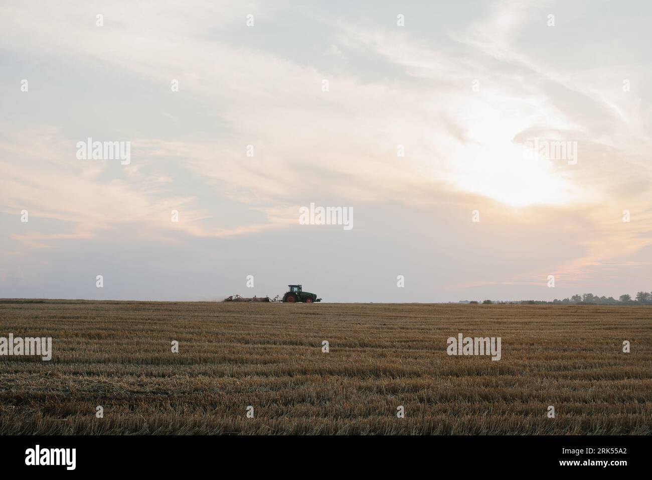A modern tractor with a heavy trailed disc harrow plows a wheat field ...