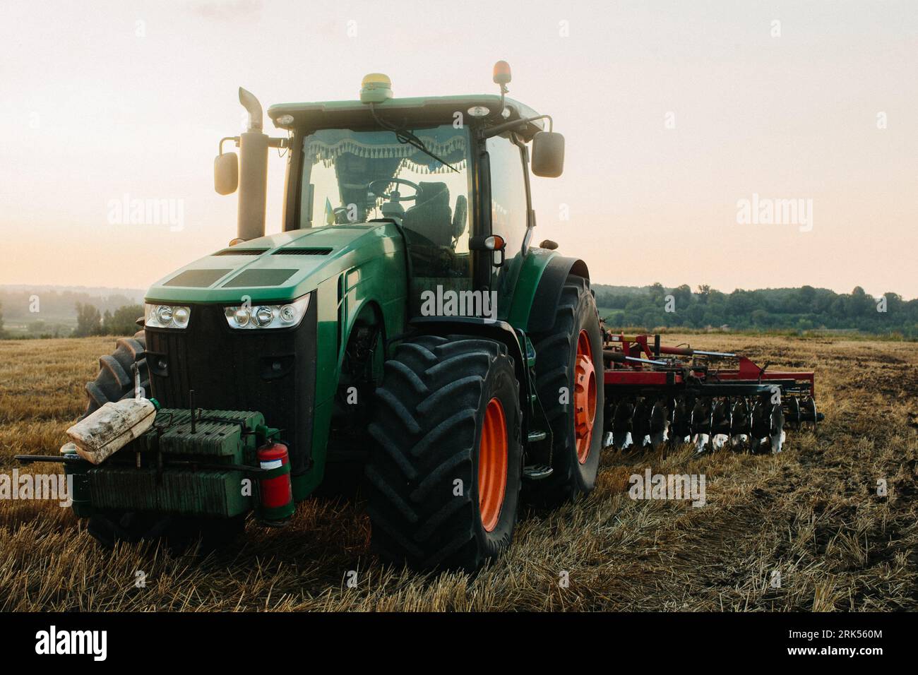 Close up photo of a modern green tractor with a red disc plow working ...