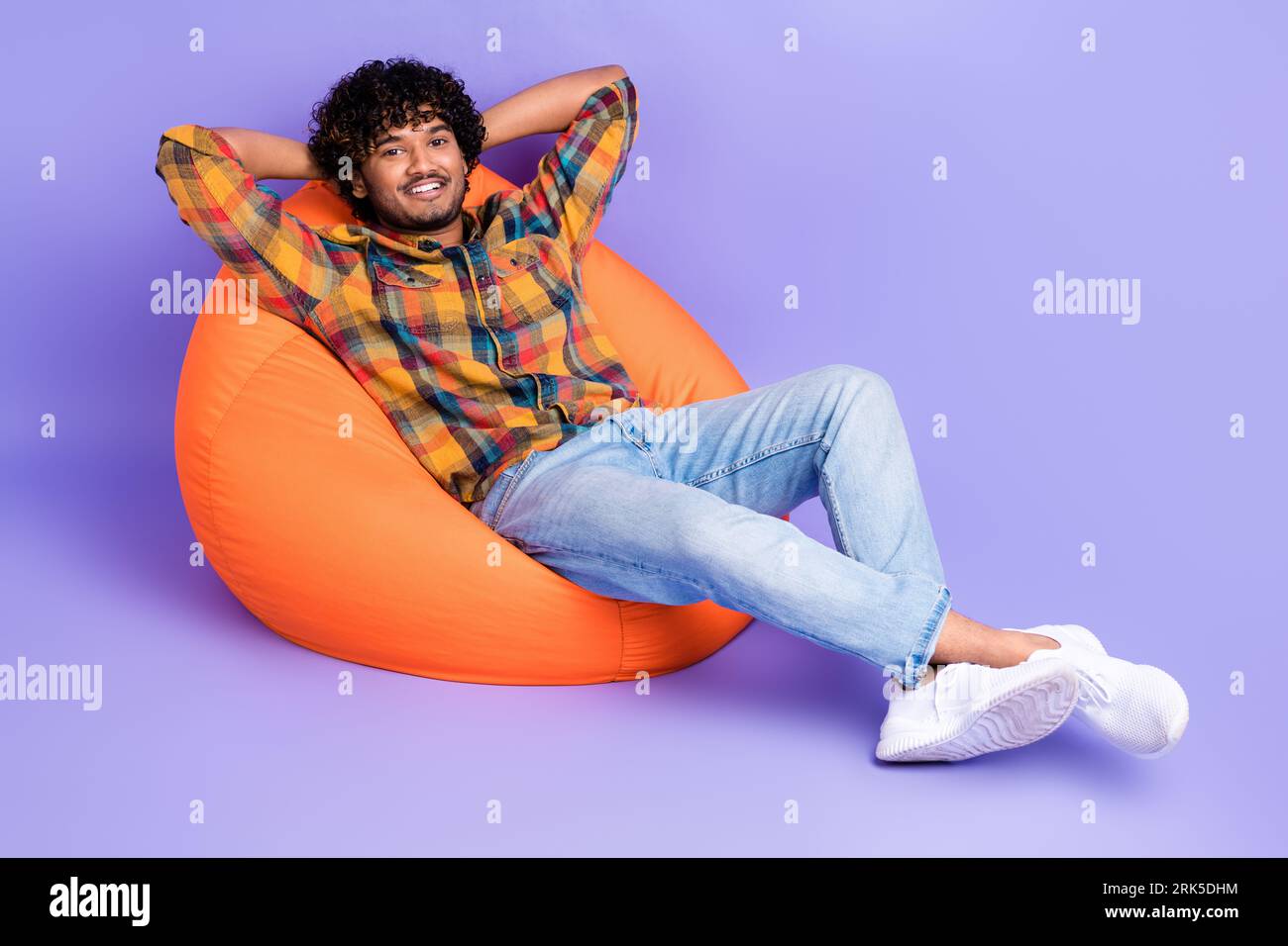 Full length photo of satisfied cool man plaid shirt lay on orange comfy ...