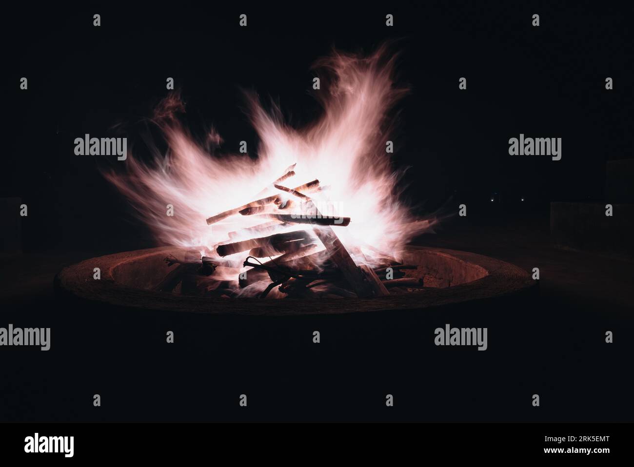 A dramatic night scene of a burning fire pit, emitting smoke and ... A dramatic night scene of a burning fire pit, emitting smoke and ...