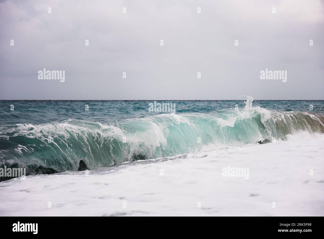 A large wave in the ocean crashing onto the shoreline, creating a white ...