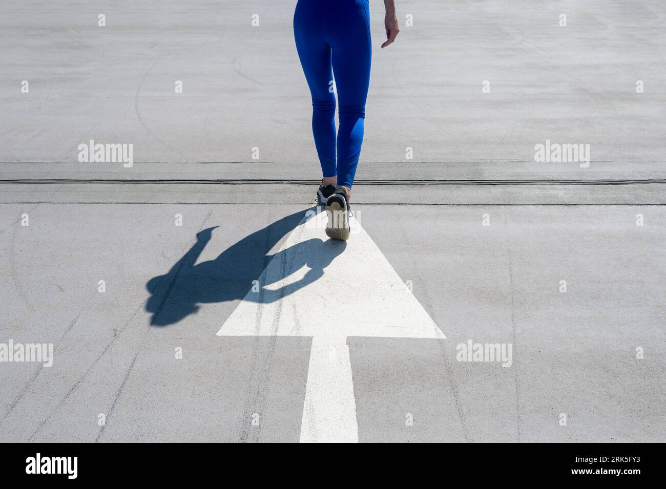 shadow of a woman athlete jogger in road, running over a painted arrow ...