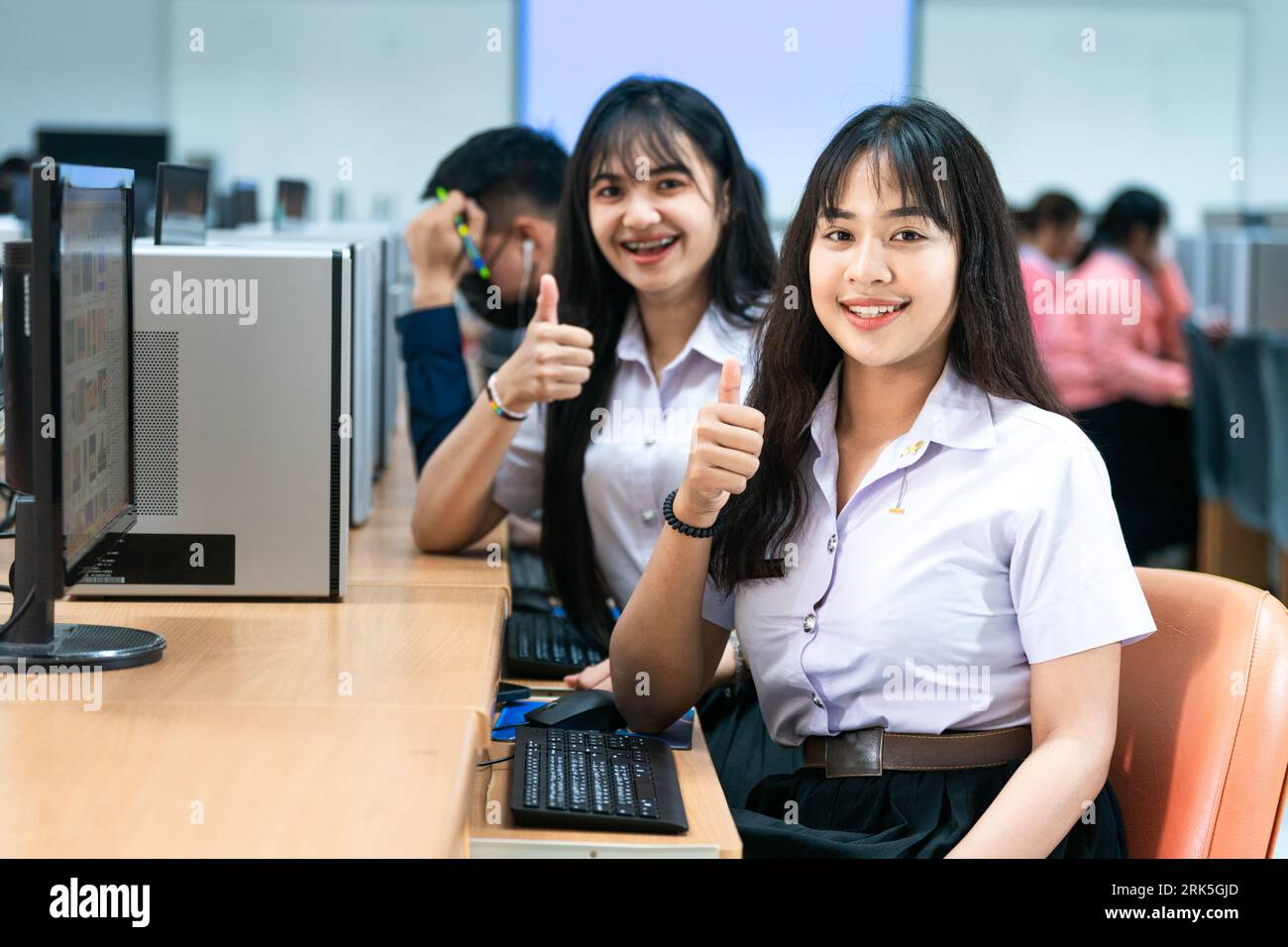 Two young Asian female students seated at a desk in front of a laptop ...