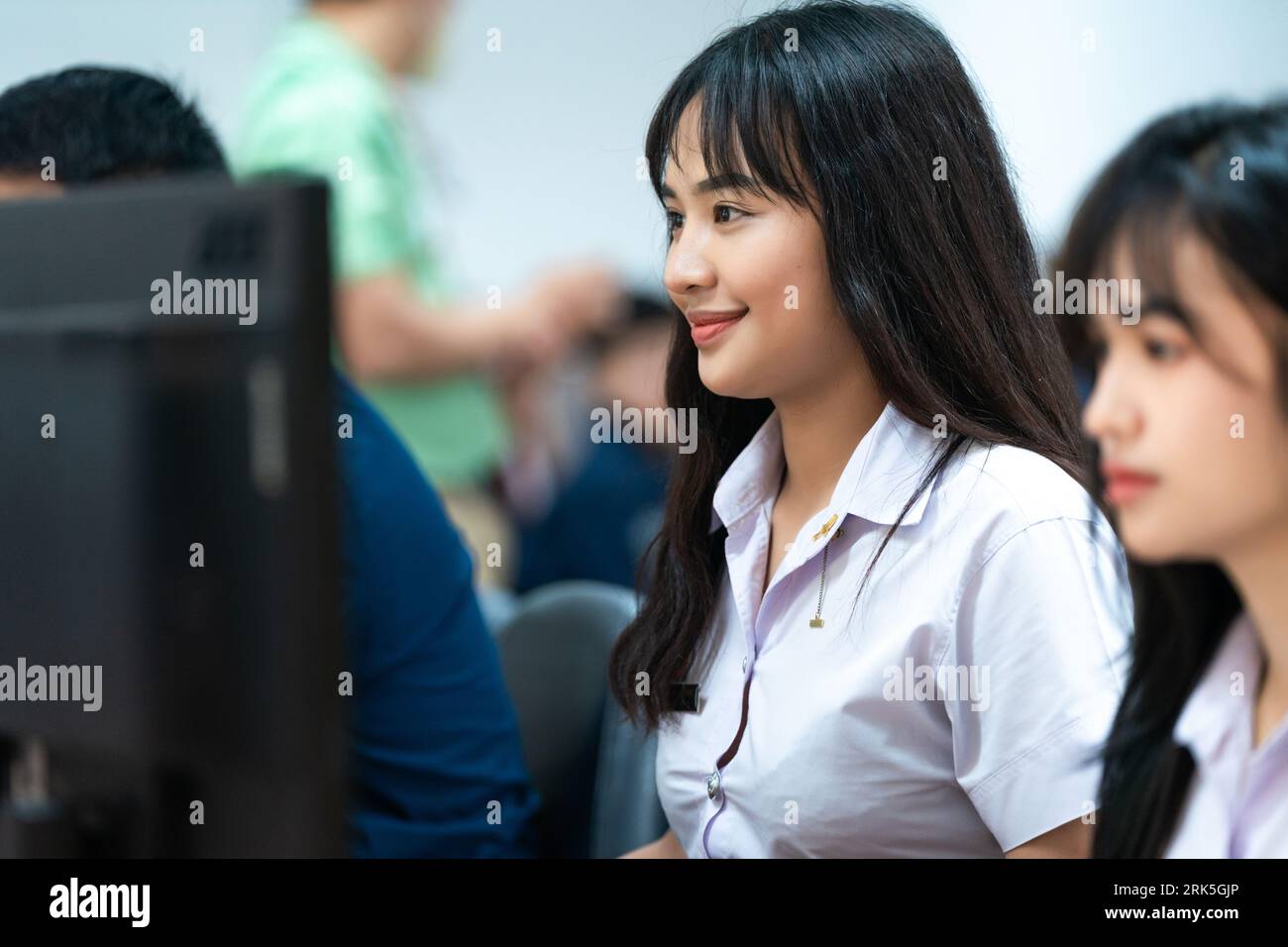 Two Asian female students are sitting in front of a computer in a ...