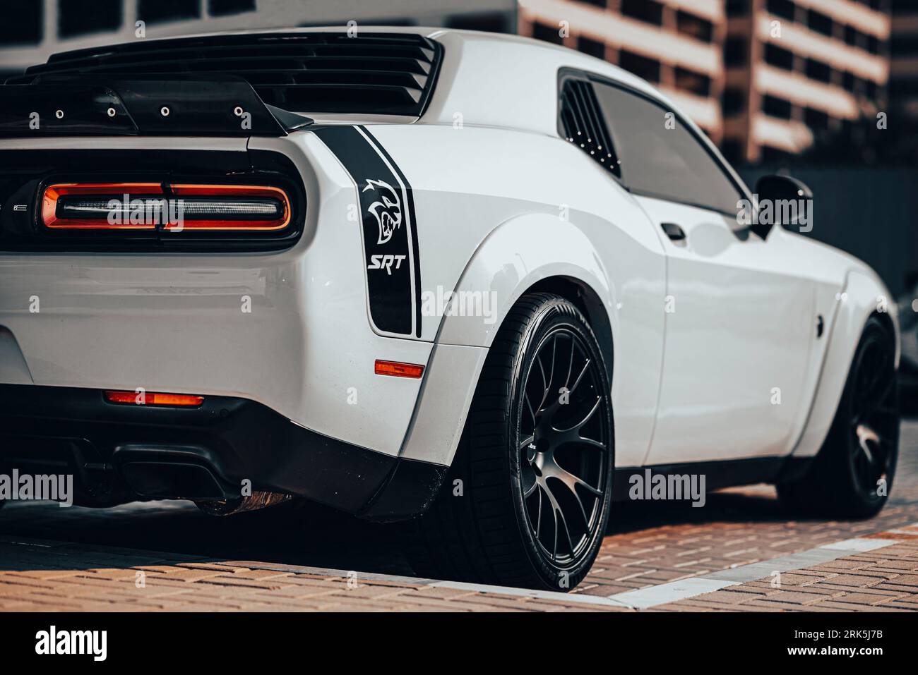 A white Dodge Hellcat SRT car is parked in front of a large building ...