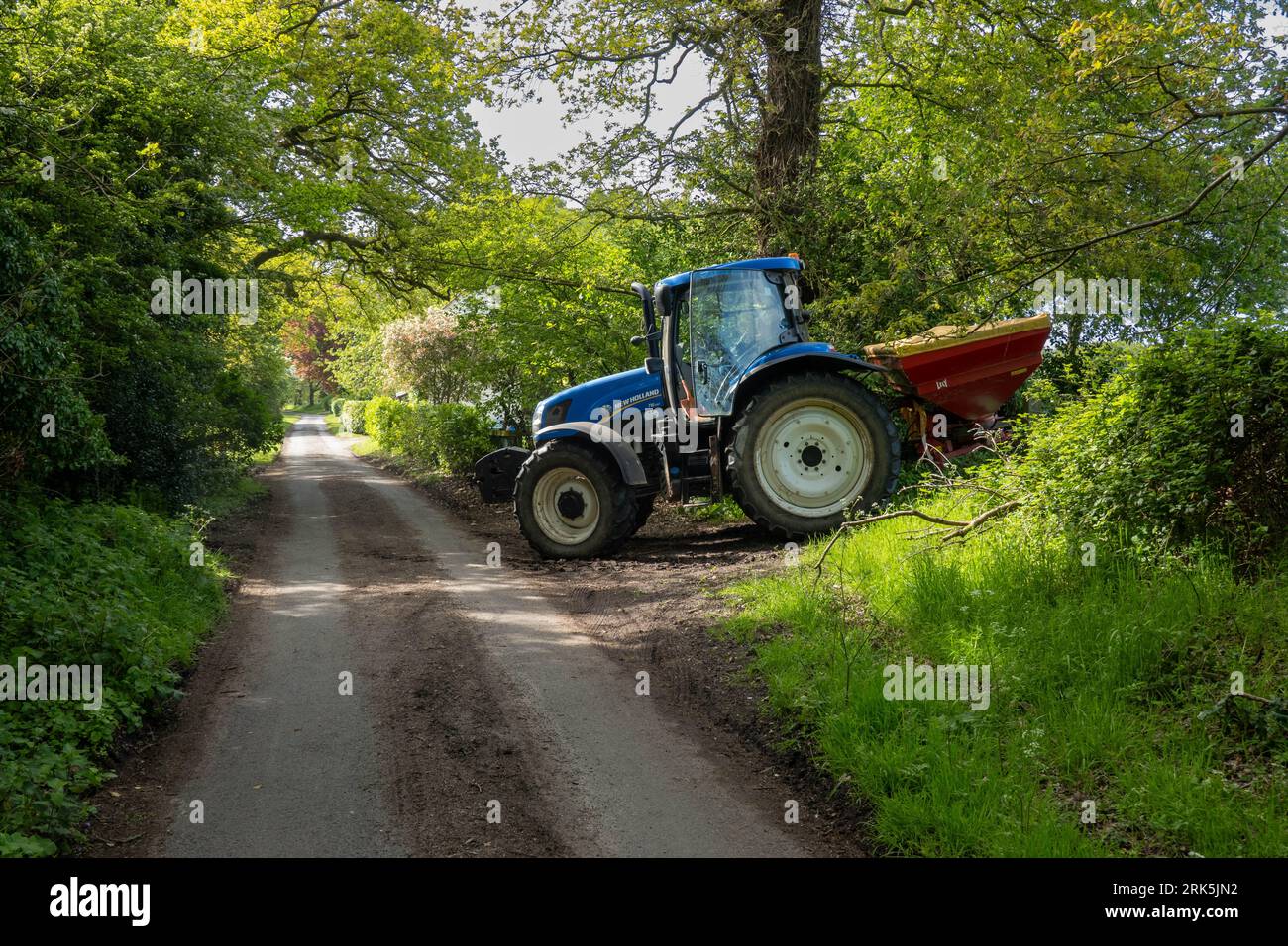 Farmer in tractor with trailer/hopper coming out of field onto narrow ...