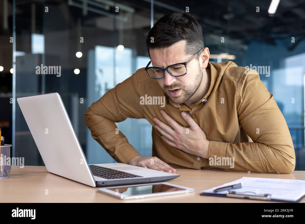 Heart attack, panic attack at work. A young man holds his chest while ...