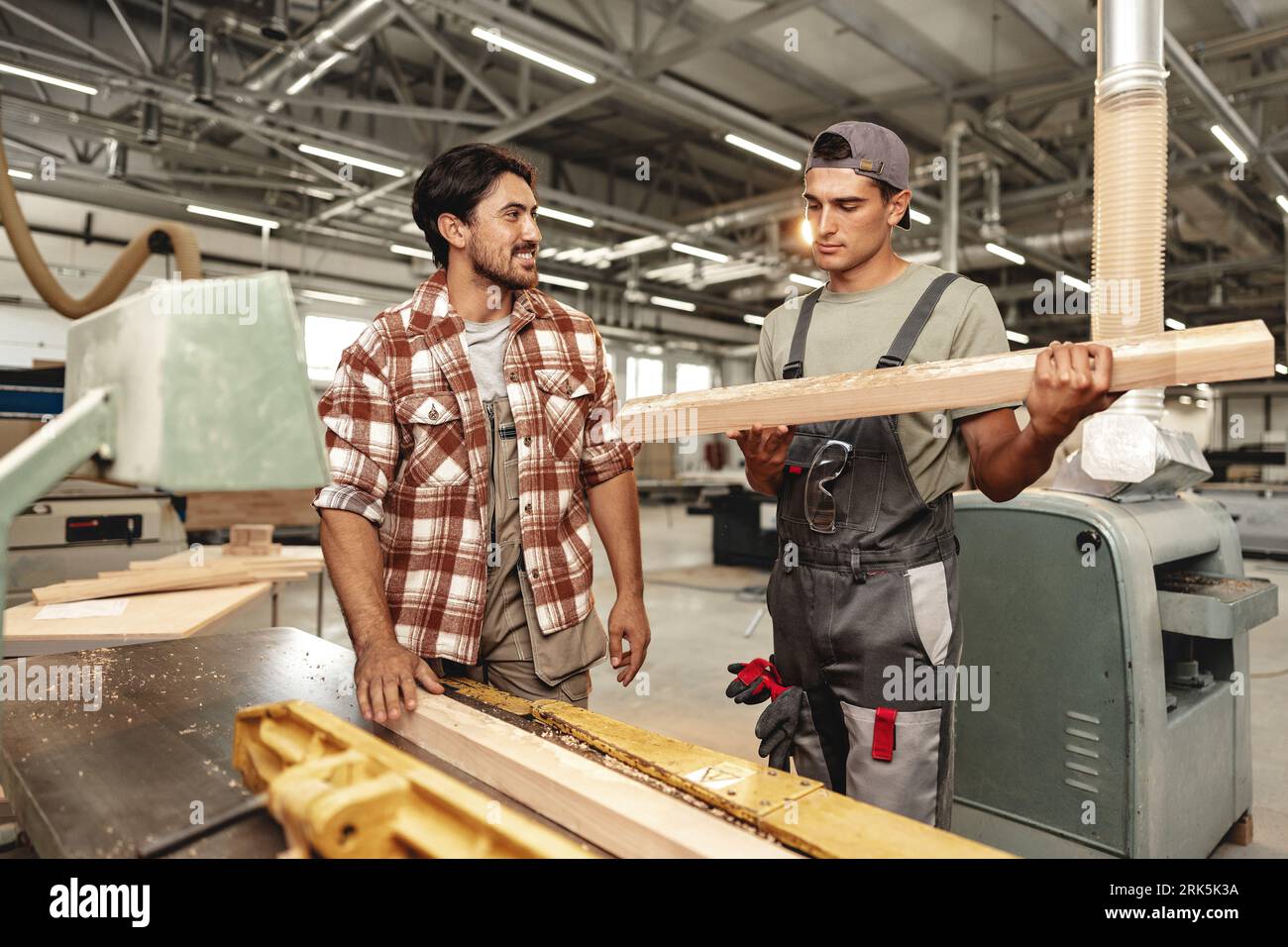 Two young carpenters working with wood standing at table in workshop ...