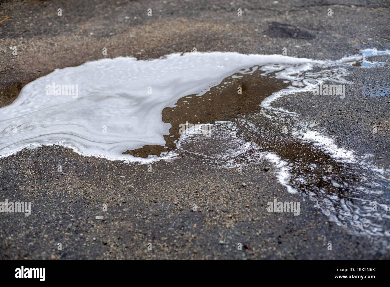 white soapy foam in gray dirty water in a puddle on the ground outside ...