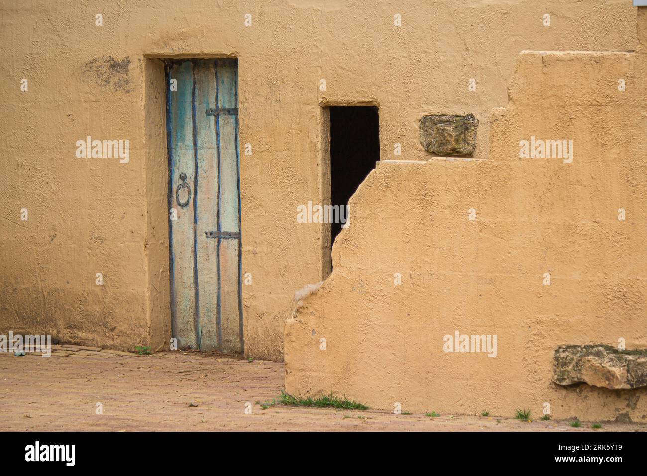 An aged adobe dwelling with a door entrance and green shutters ...
