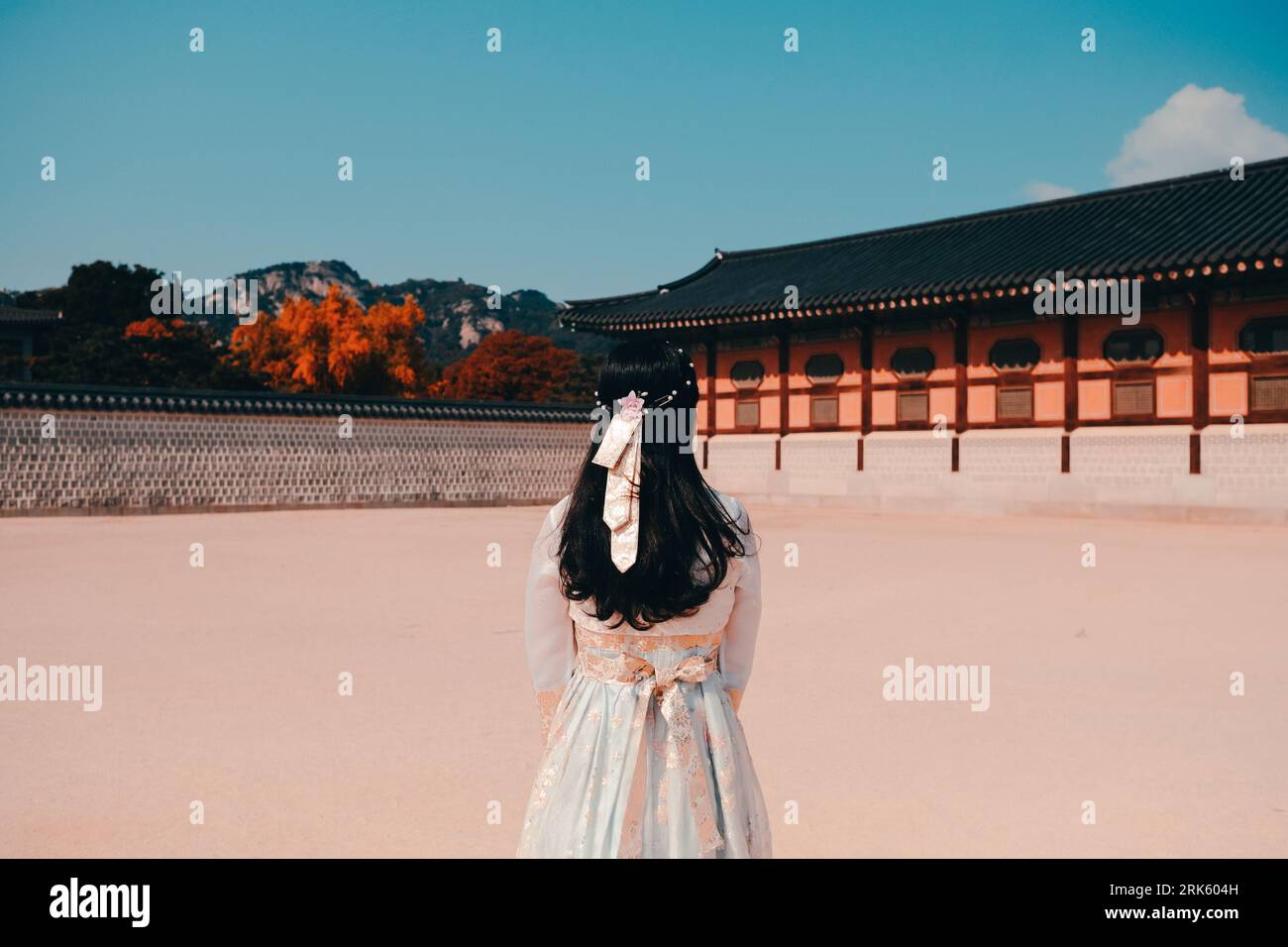 A young female stands in a grand palace courtyard in the fall season ...
