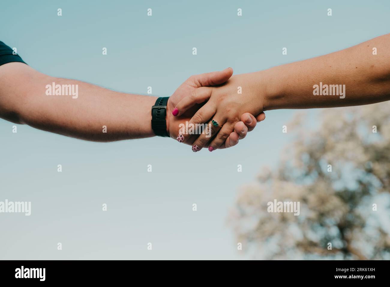 Two hands clasped in agreement against a serene blue sky background ...