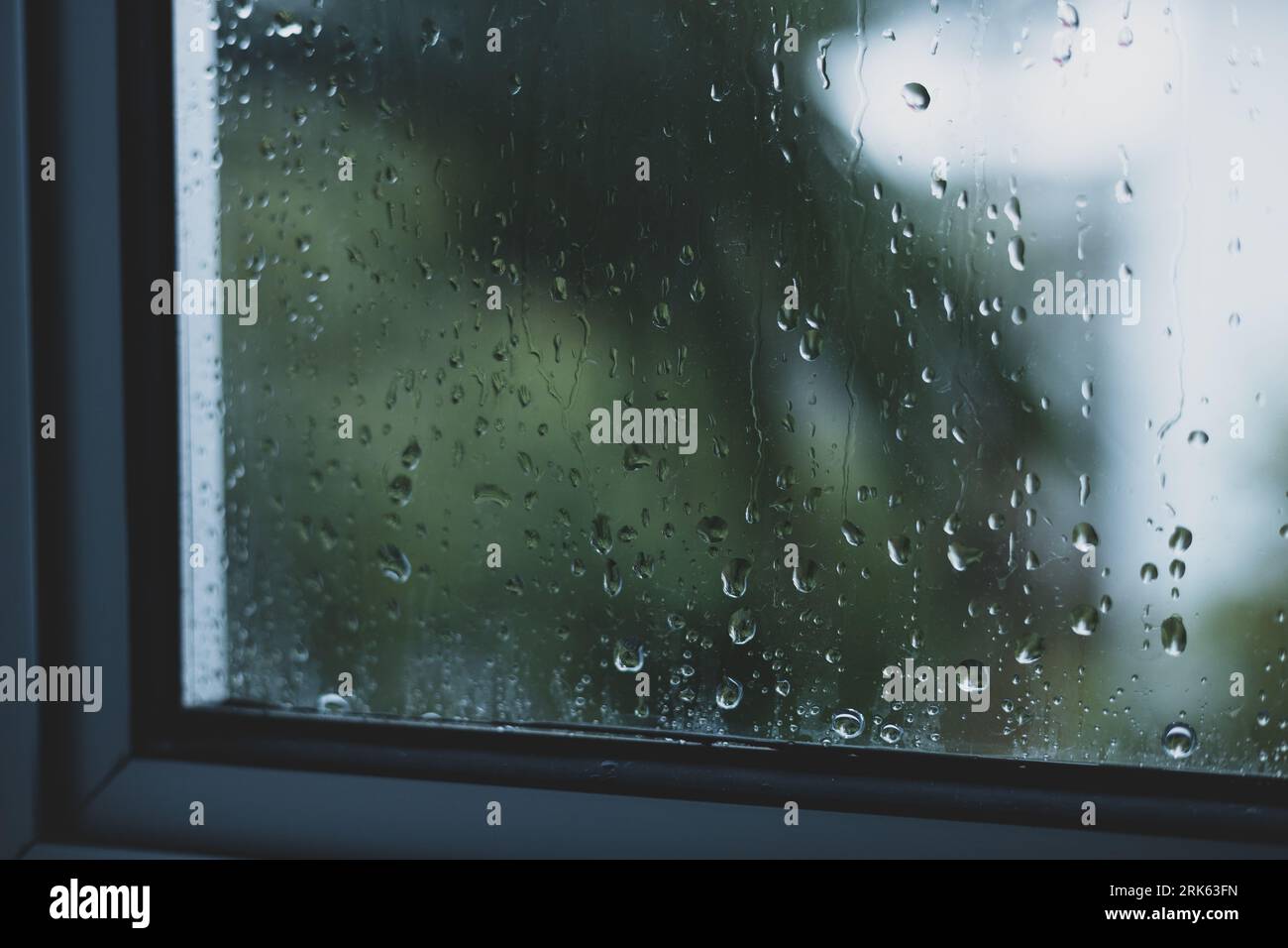 A close-up image of a window pane with water droplets running down the ...