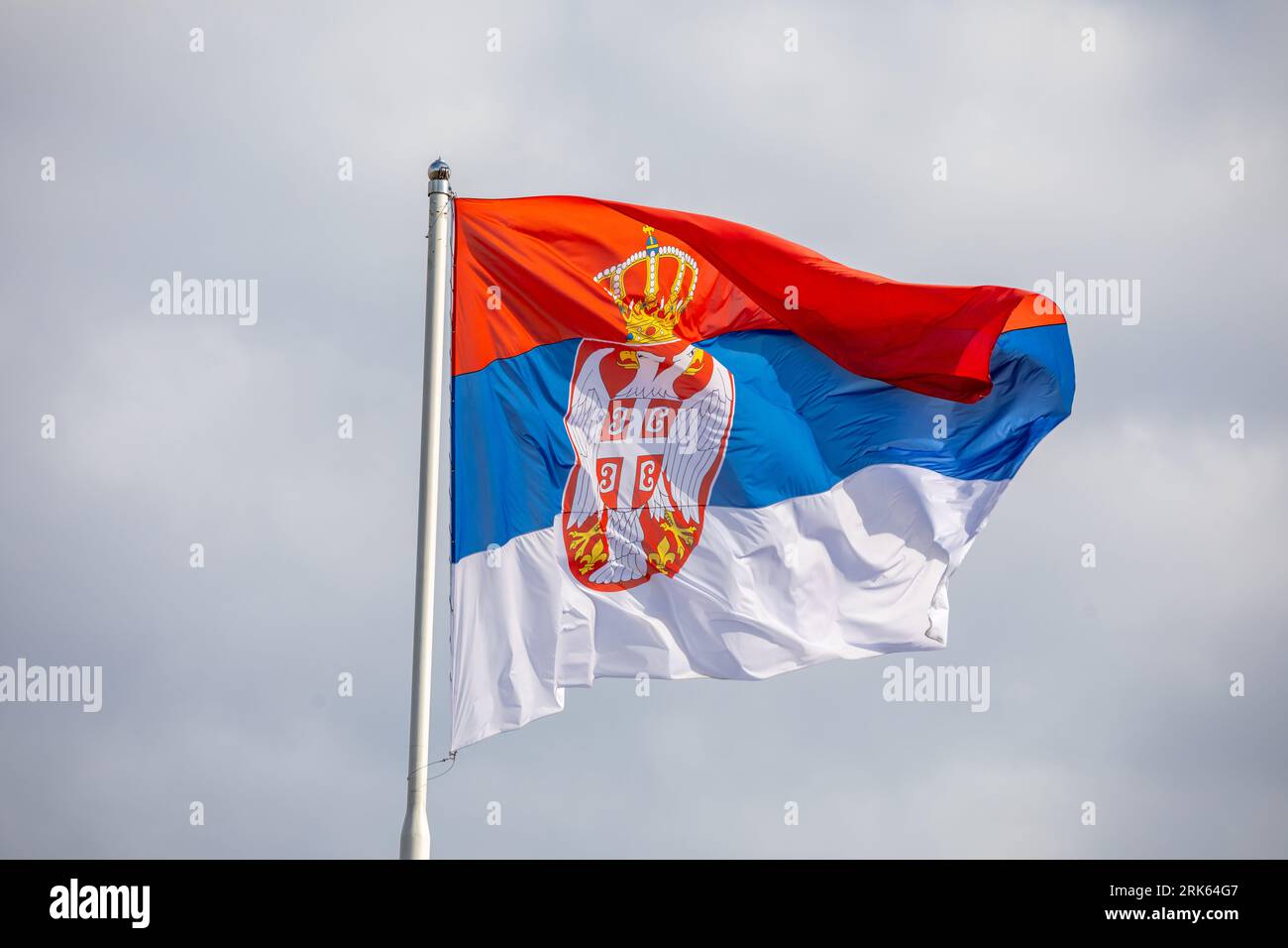 Serbian national flag on wind, outdoor, cloudy background Stock Photo ...