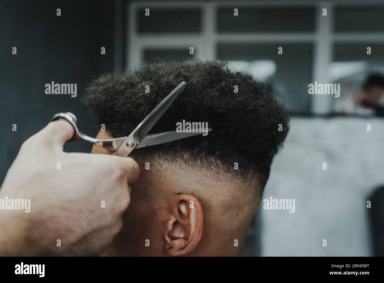 A male barber expertly combs and styles the hair of a customer sitting ...