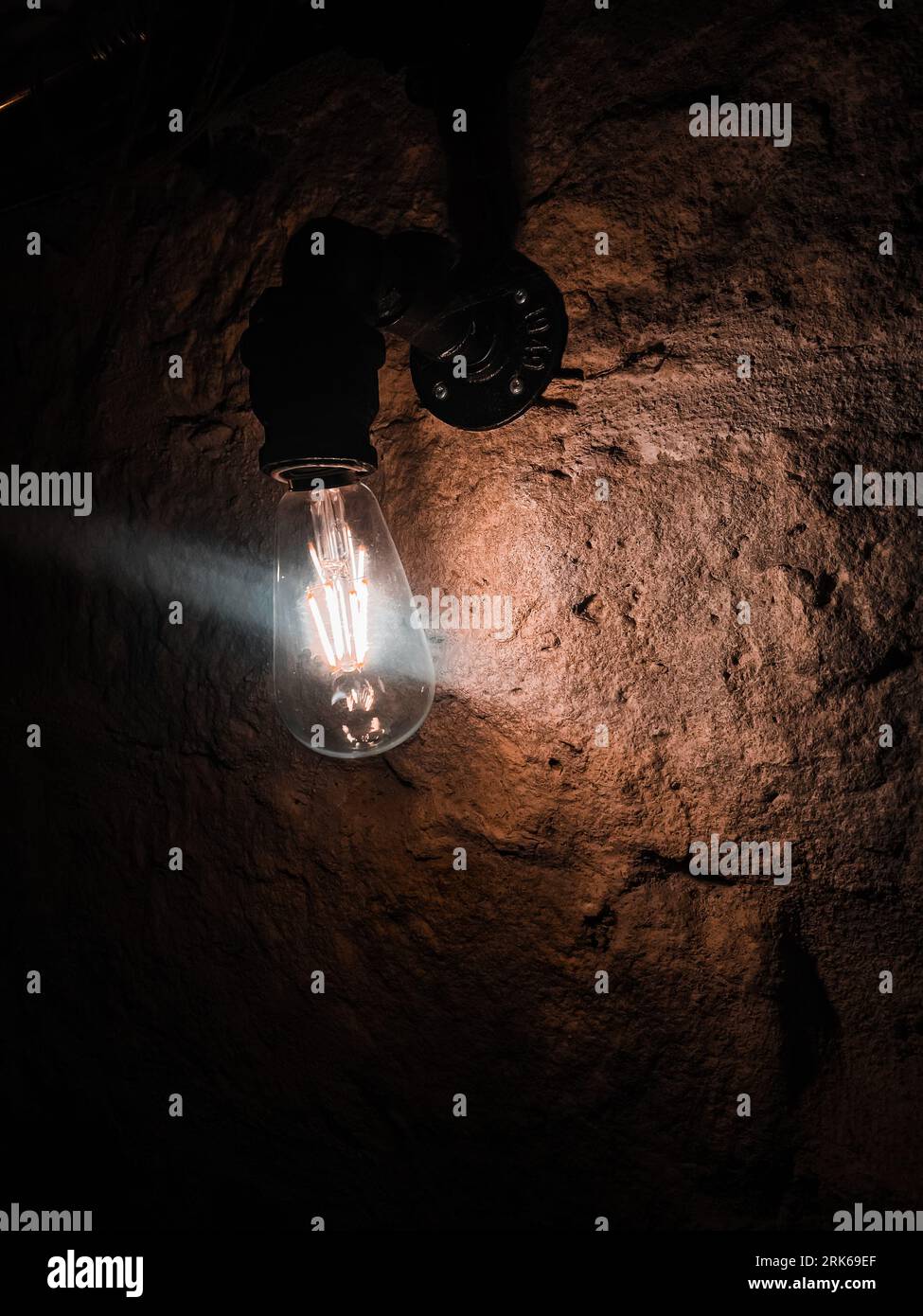 A modern lightbulb illuminated on top of a rustic stone wall ...