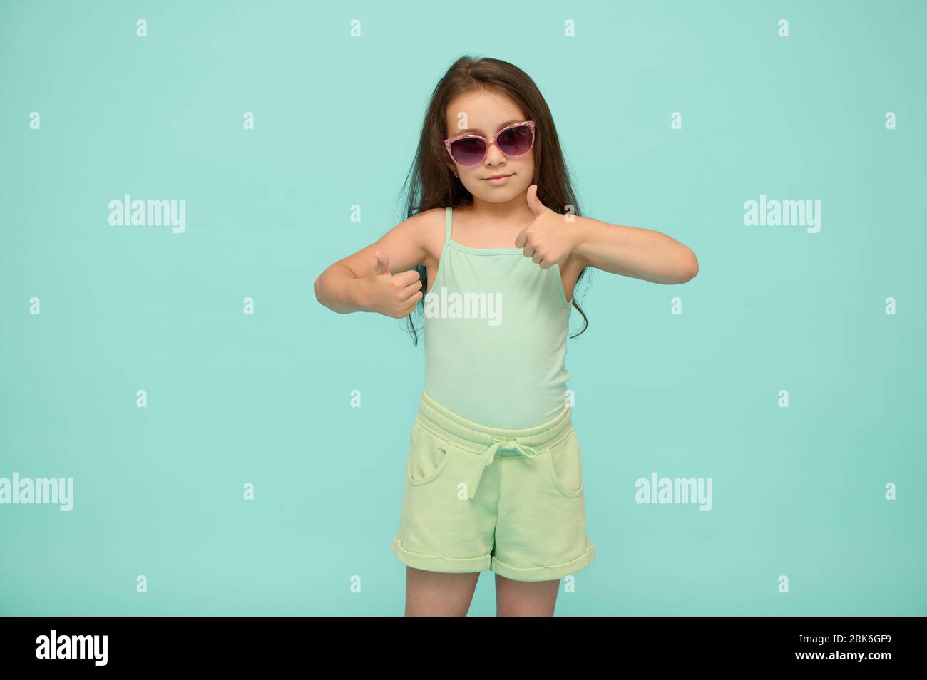 Lovely little kid girl in summer clothes and sunglasses, gestures with ...