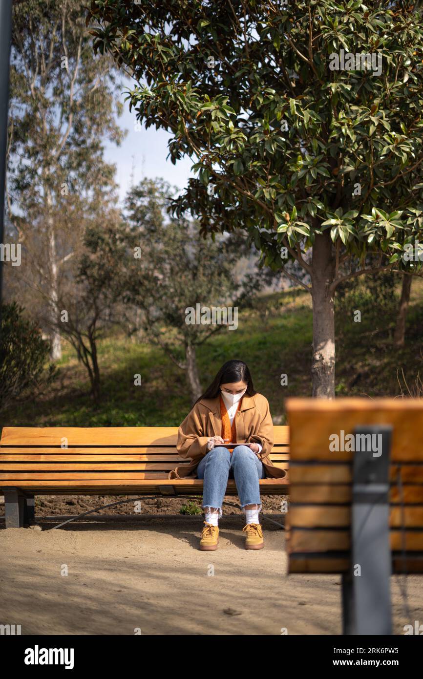 A young woman with a disability sitting on a park bench using a digital ...
