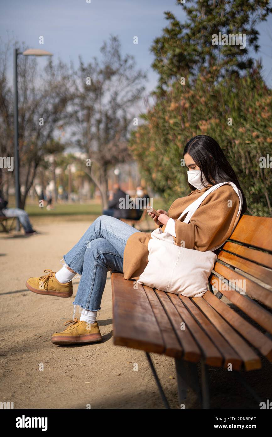 A young woman with a disability sitting on a park bench using a digital ...