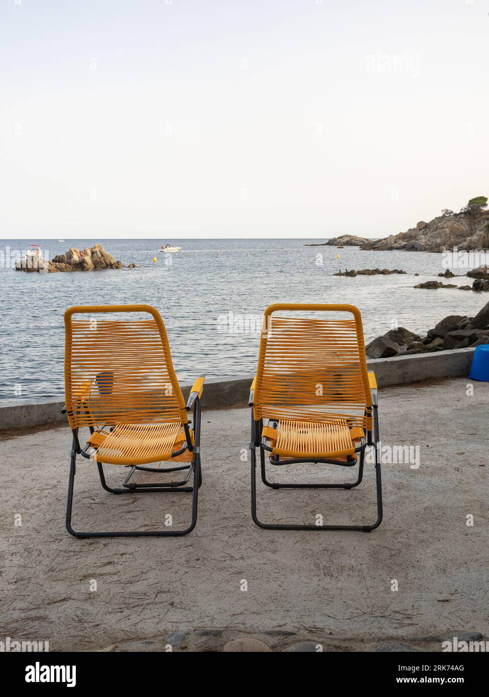 Two beach chairs are situated facing the ocean at sunset, providing an ...