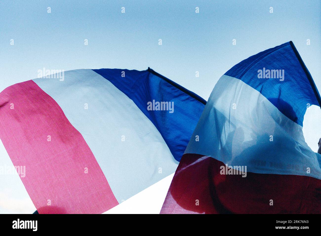 The two flags of France blowing in the wind against a blue sky backdrop ...