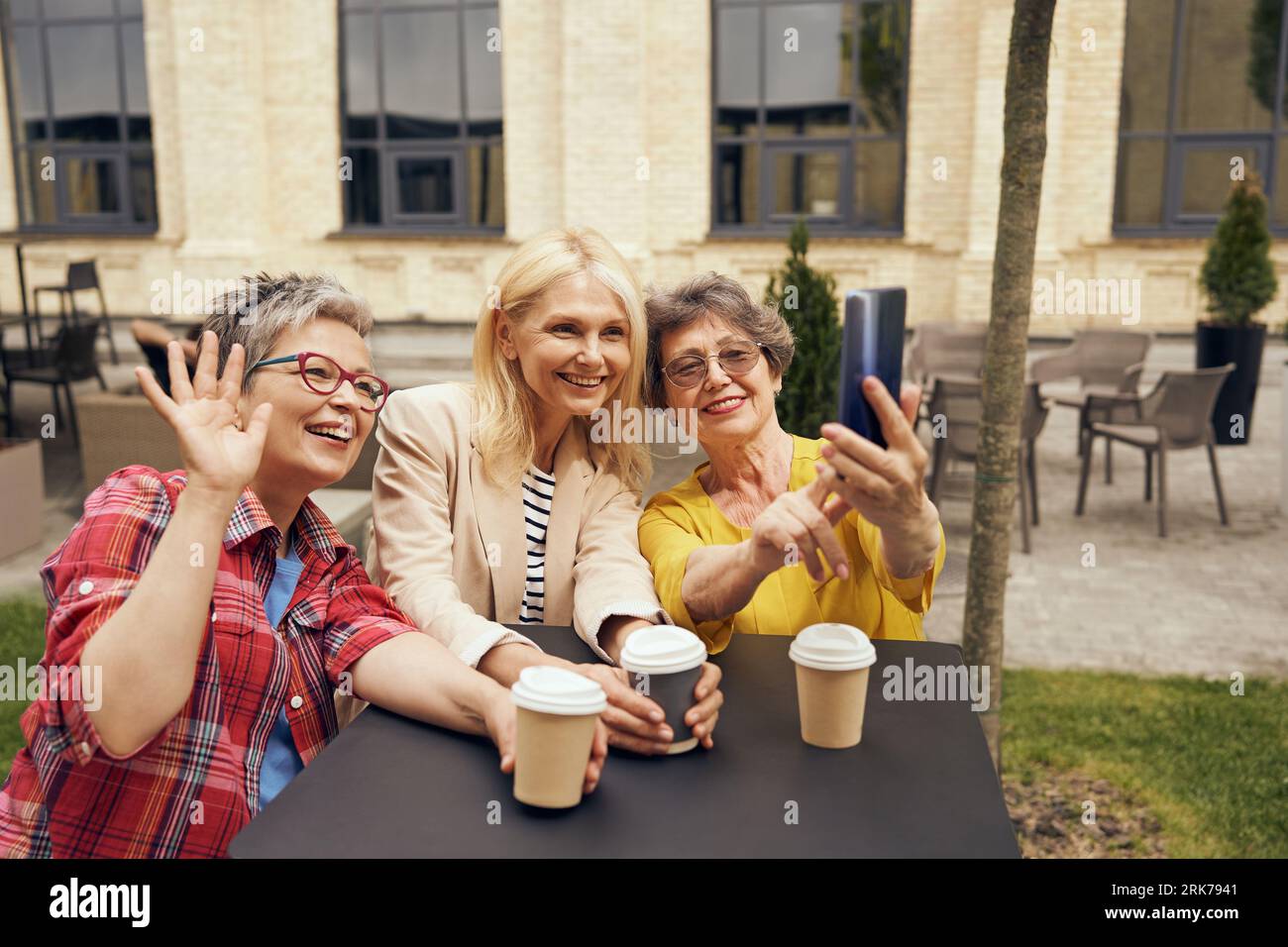 Smiling mature ladies sitting in cafe terrace and talking via video ...