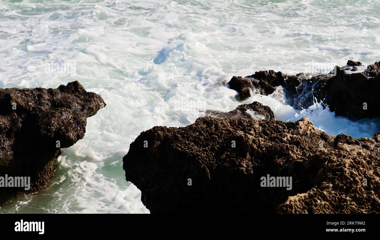 Splashes of the foamy sea water between porous rocks Stock Photo - Alamy