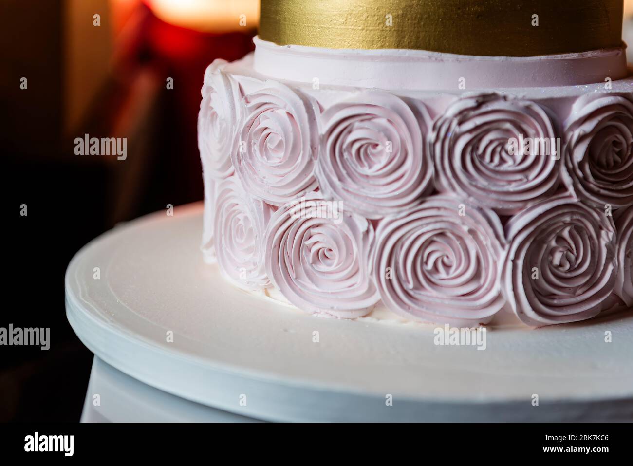 A decadent three-tier cake decorated with pink roses and gold leaf ...