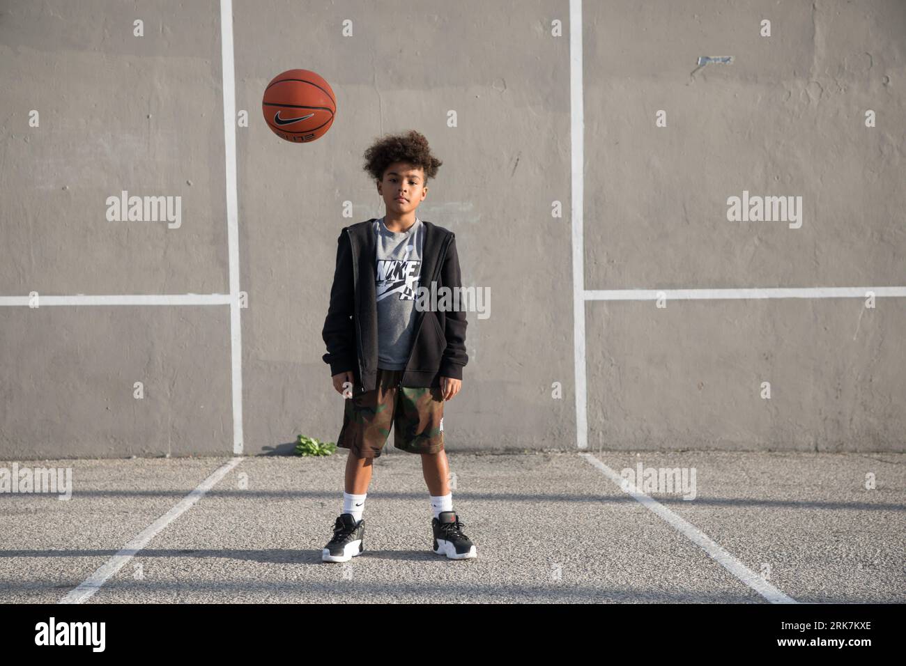 A cheerful young male stands outdoors, throwing a basketball up into ...