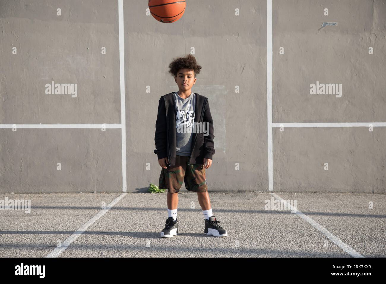 A cheerful young male stands outdoors, throwing a basketball up into ...