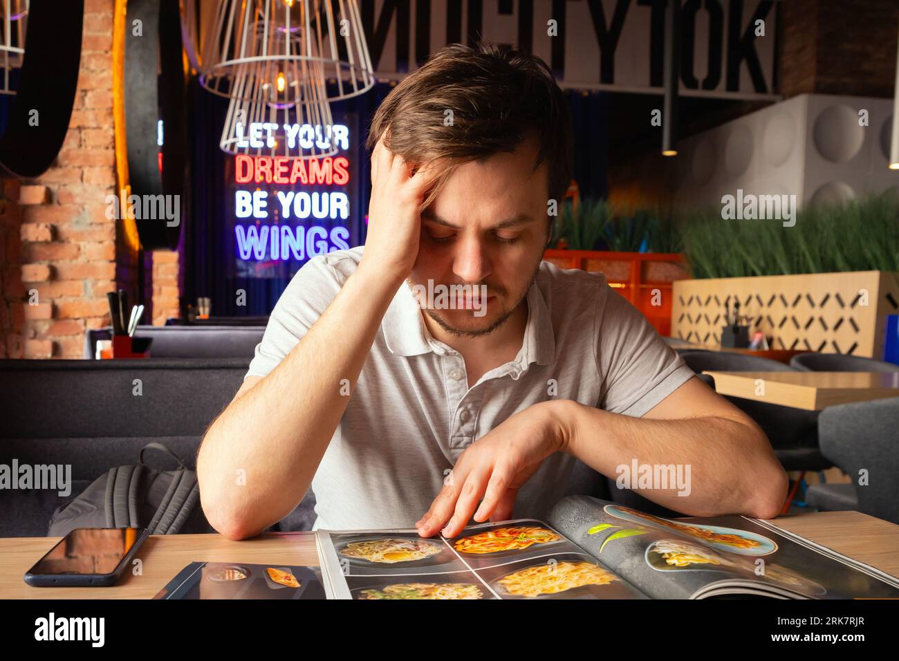young caucasian male man reading menu in restaurant. difficult choice ...