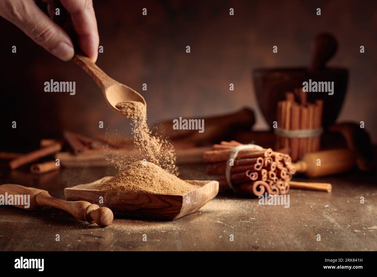 Cinnamon powder is poured into a wooden bowl. In the background are ...