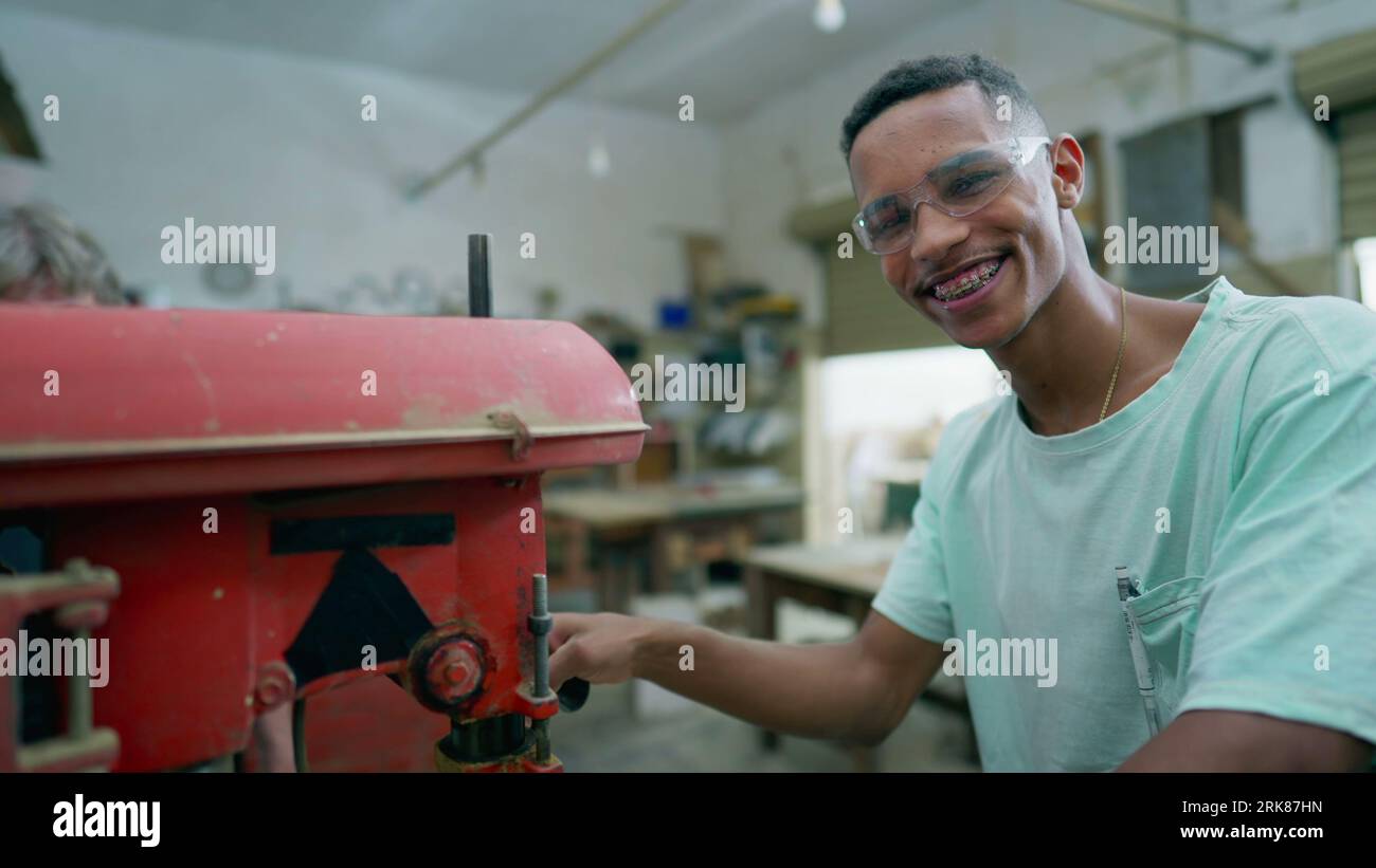 One happy young black carpentry apprentice using industrial machine ...
