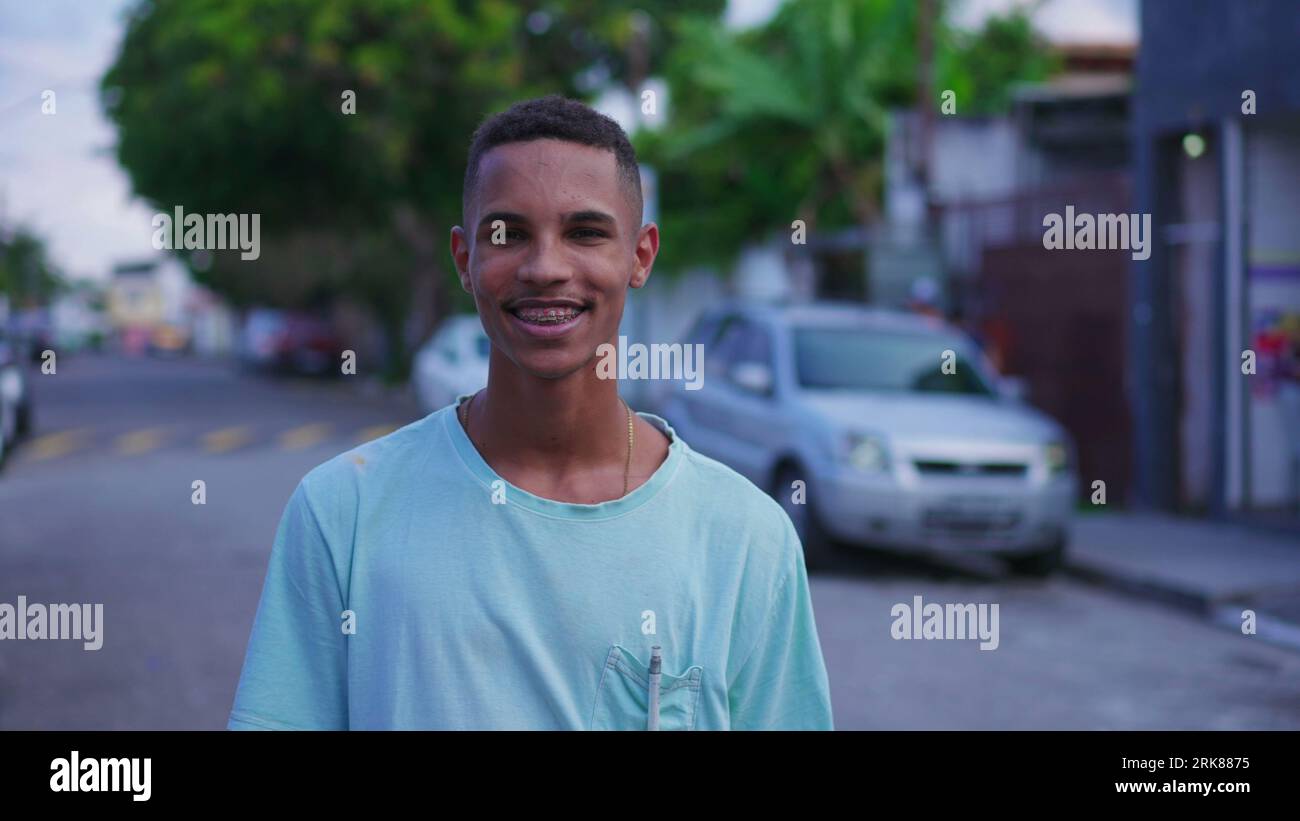 One cheerful black Brazilian young man standing in street smiling at ...